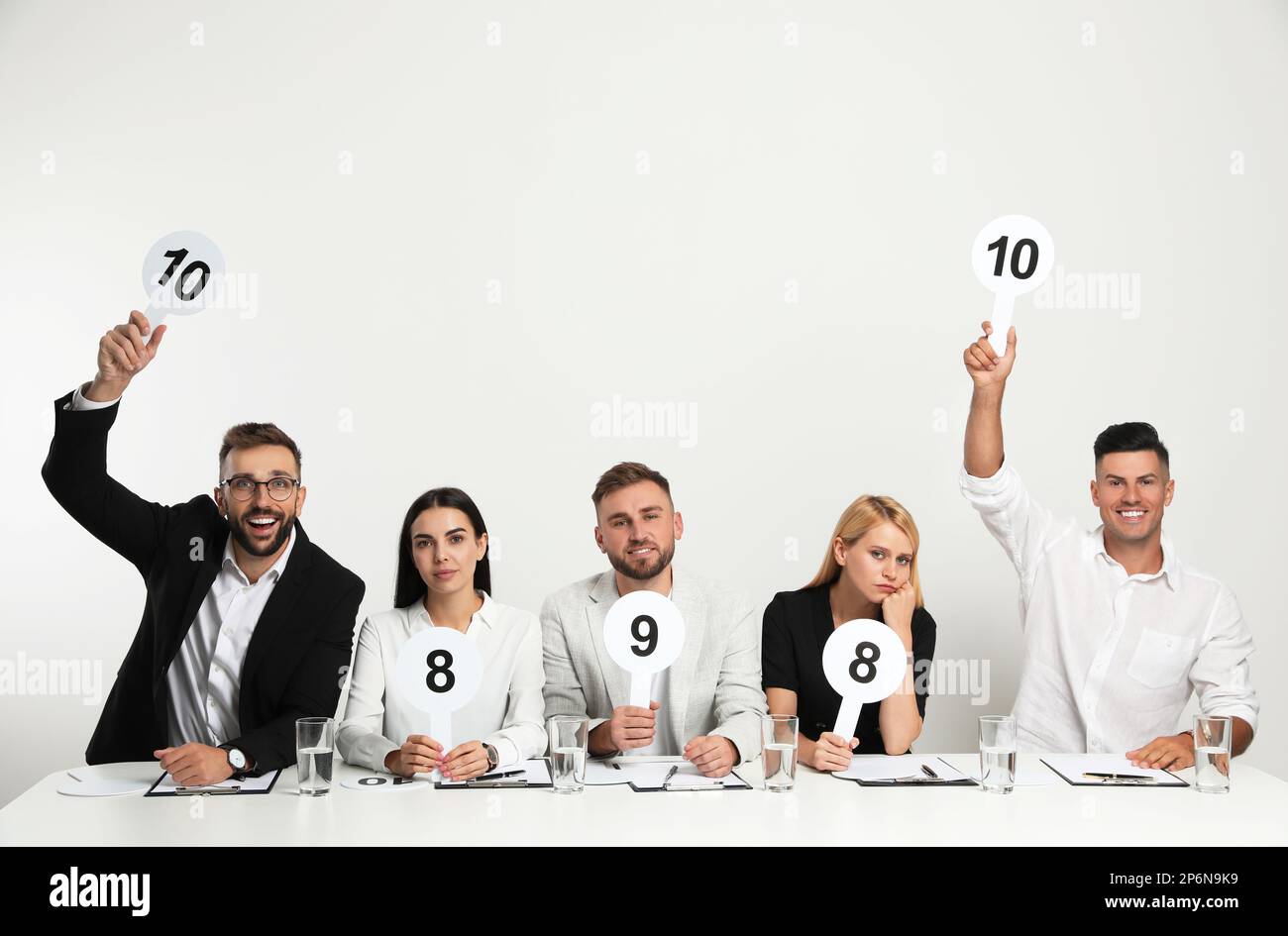 Panel of judges holding different score signs at table on white ...