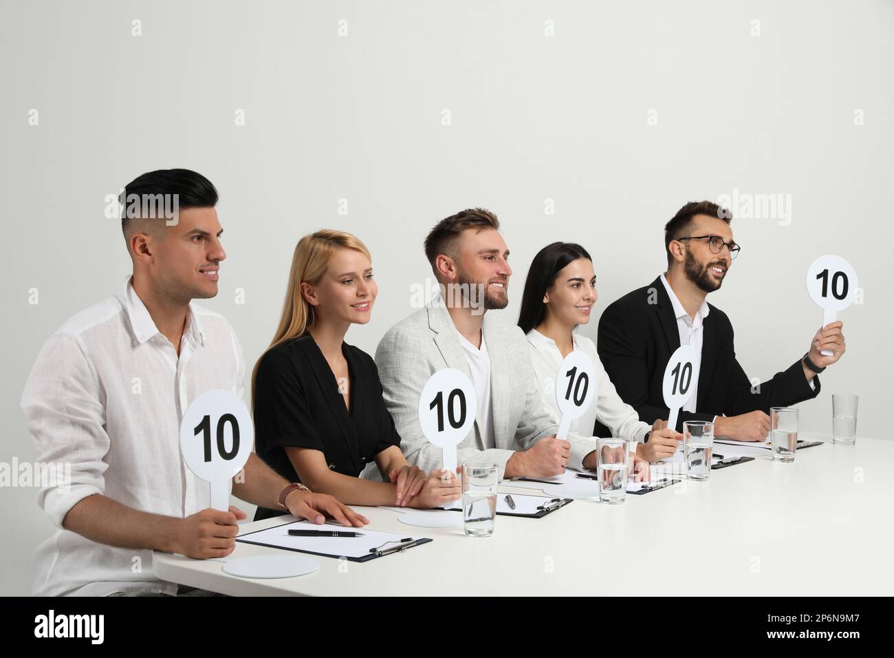 Panel of judges holding signs with highest score at table on white ...