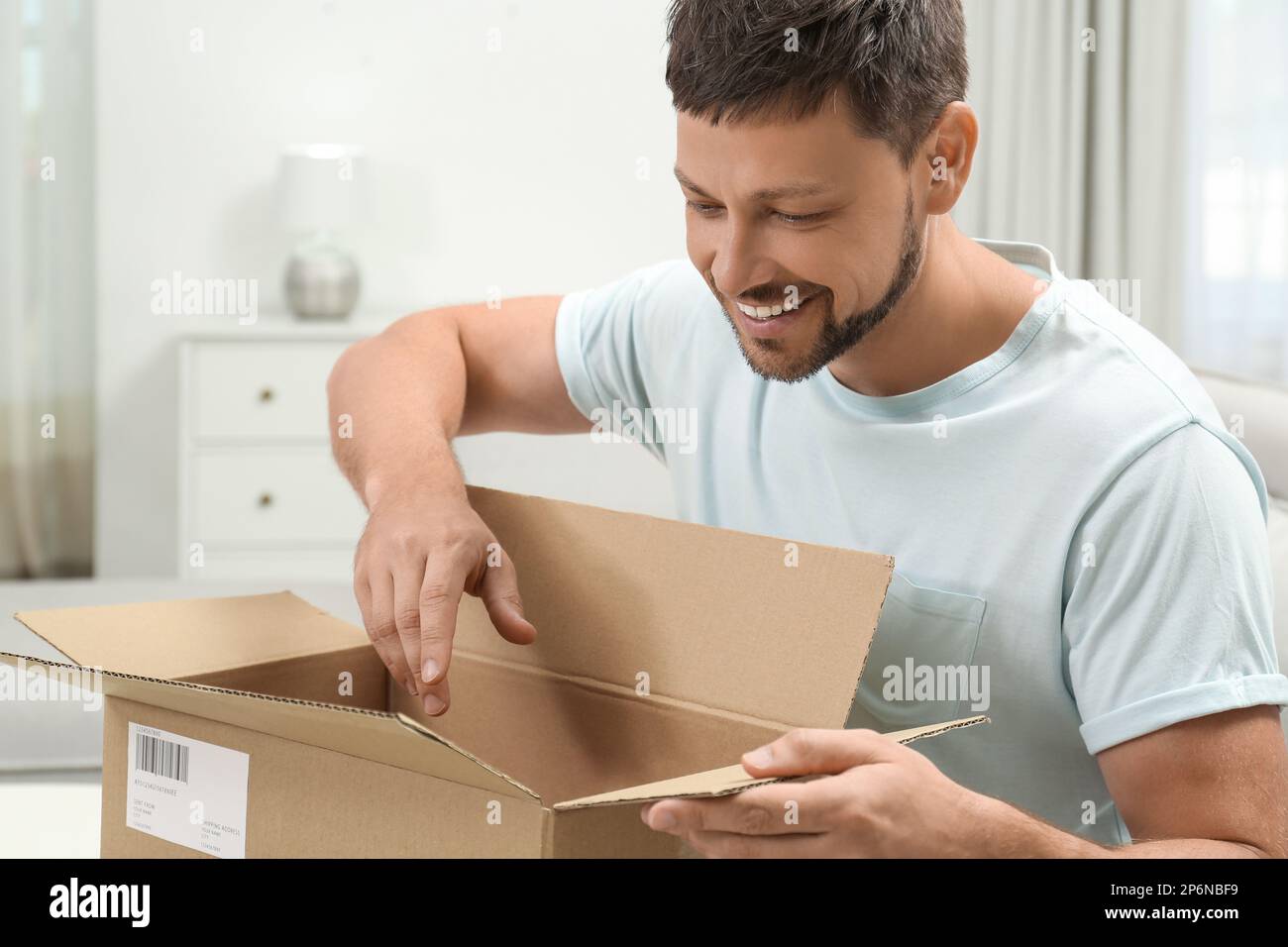 Happy man opening parcel at home. Internet shopping Stock Photo - Alamy