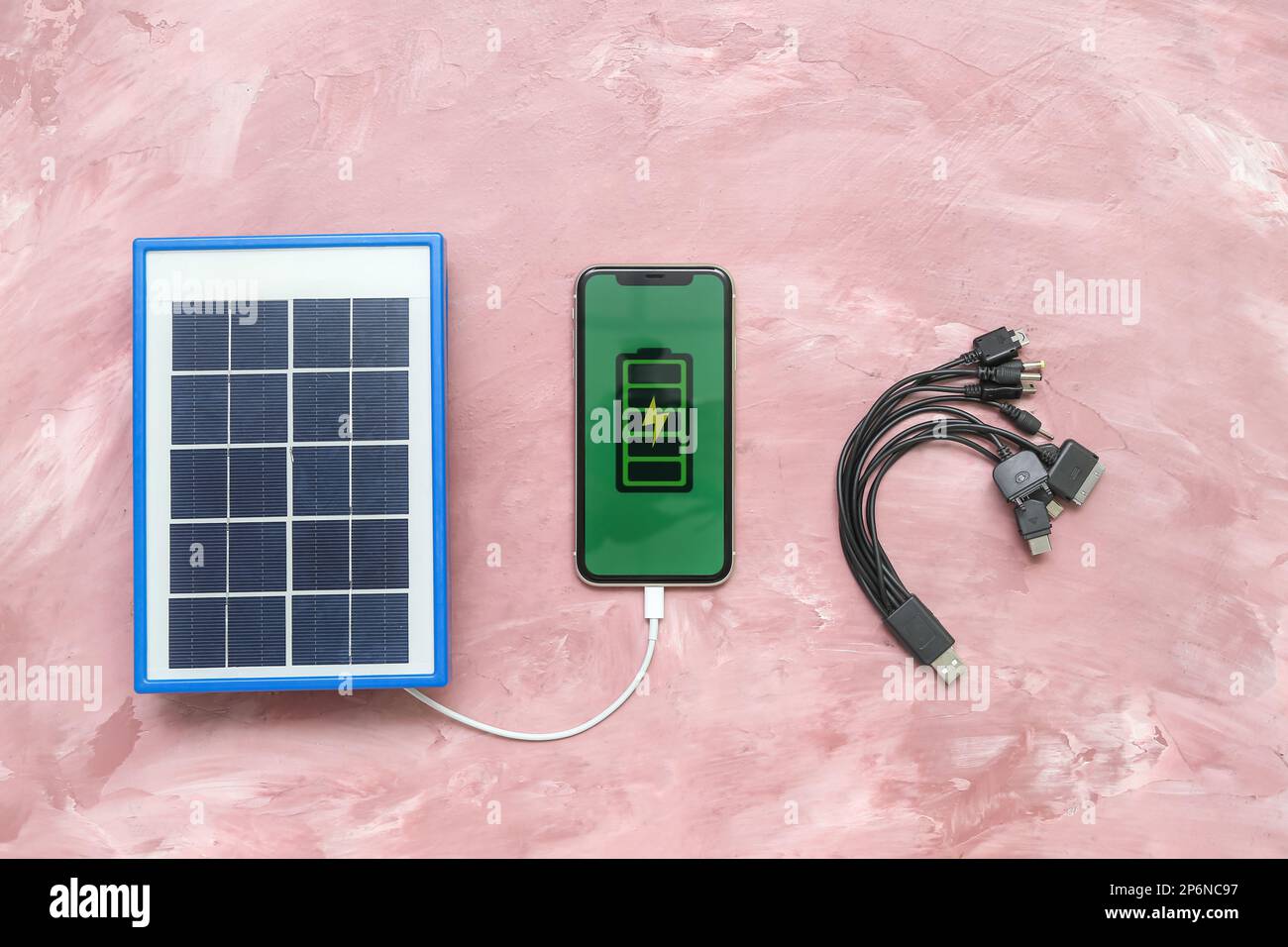 Portable solar panel charging mobile phone and different cables on pink ...