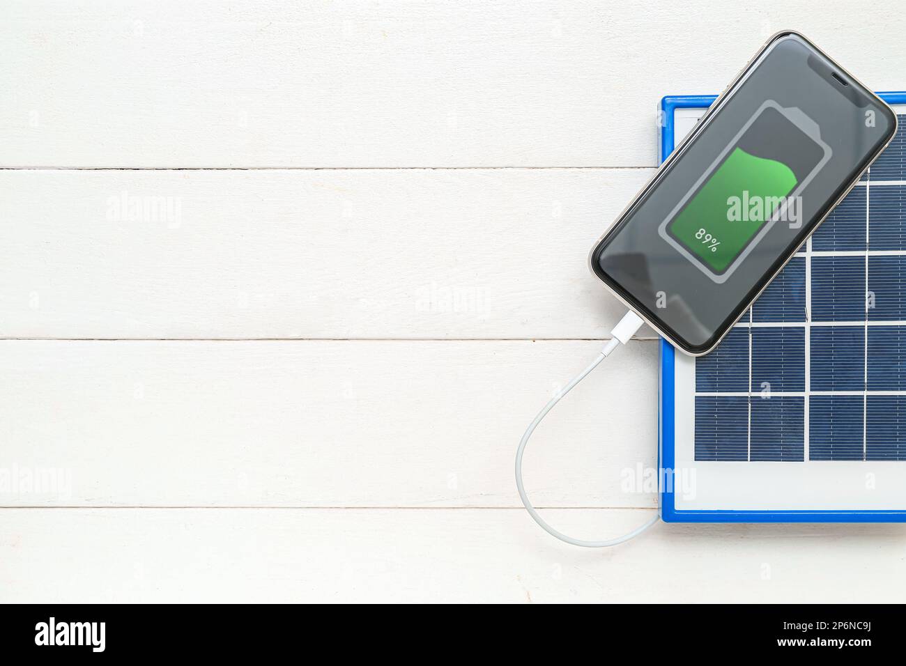 Portable solar panel charging mobile phone on white wooden background ...
