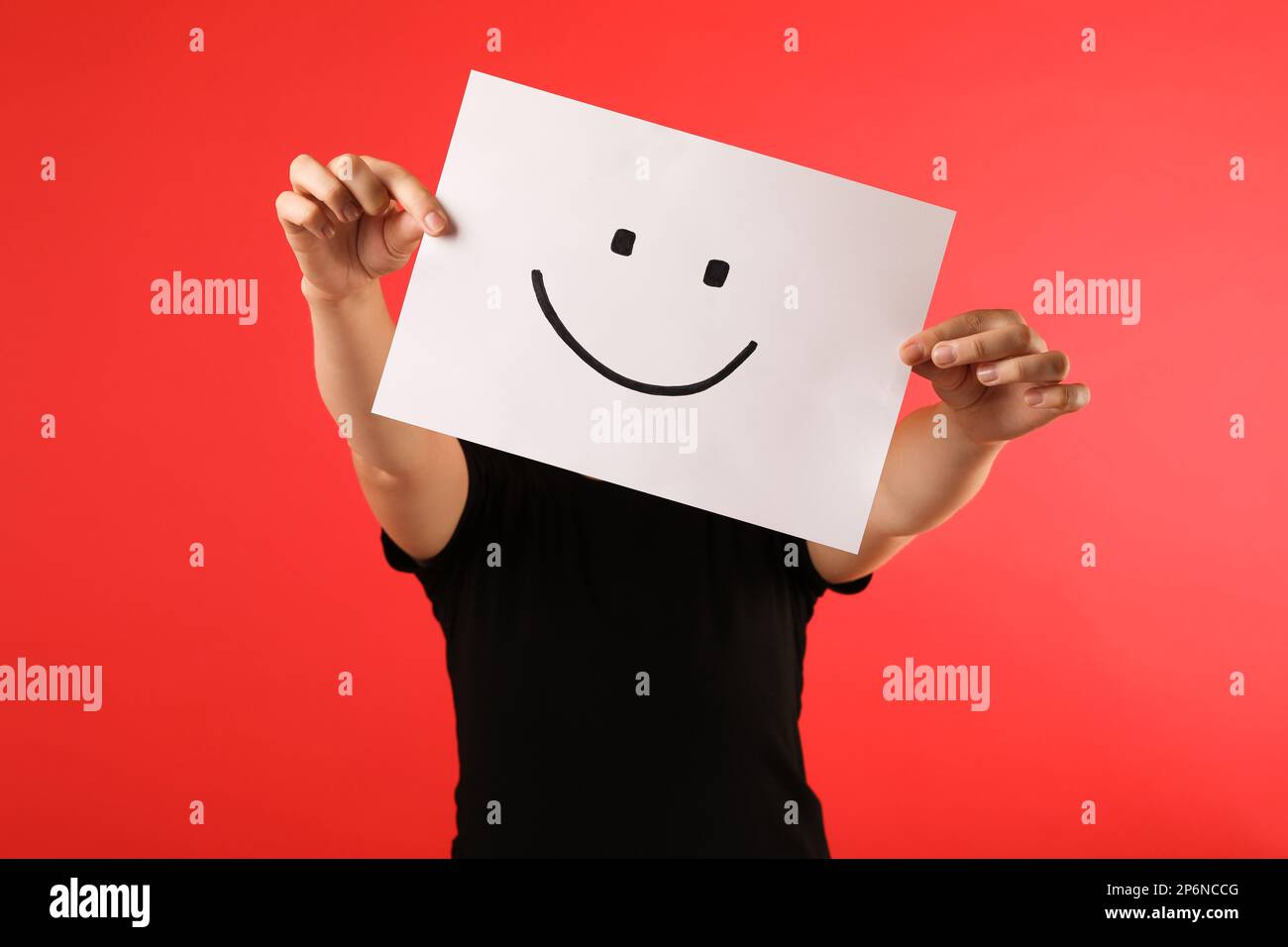 Woman hiding behind sheet of paper with happy face on red background ...