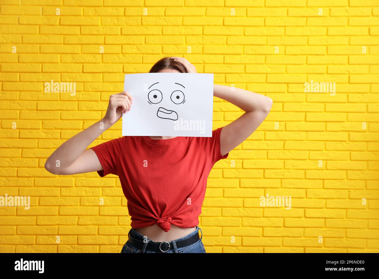 Woman hiding behind sheet of paper with scared face near yellow brick ...
