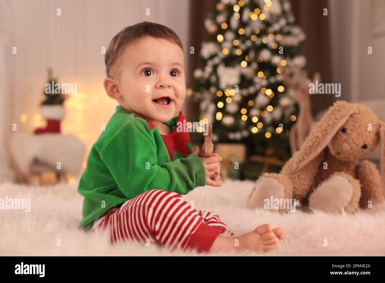 Baby wearing cute elf costume on floor in room decorated for Christmas ...