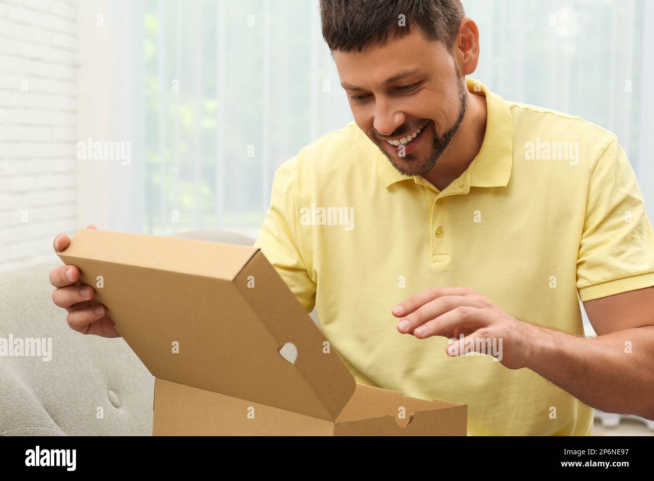 Happy man opening parcel on sofa at home. Internet shopping Stock Photo ...