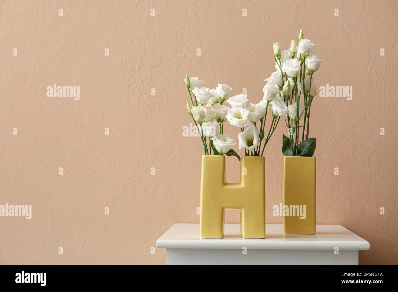 Vases in shape of word HI with beautiful eustoma flowers on table near ...