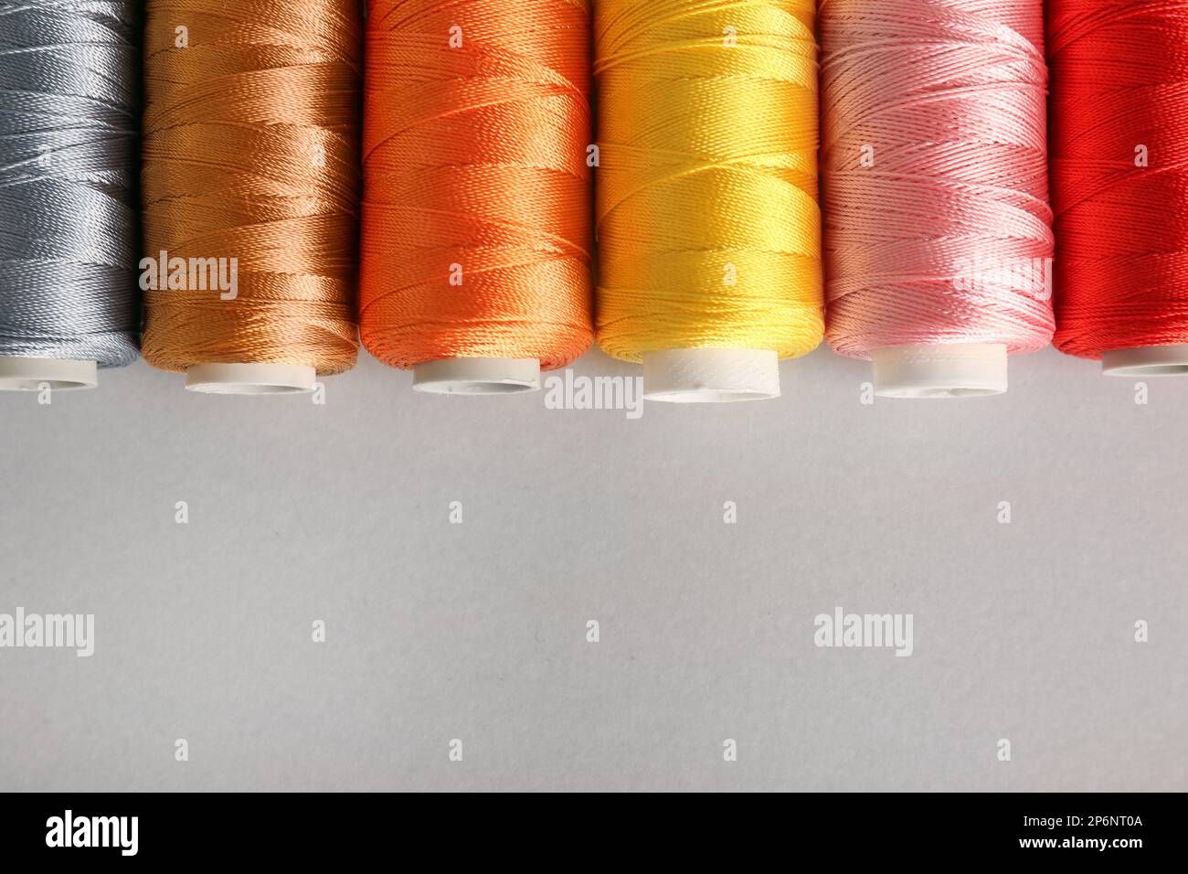 Different colorful sewing threads on light grey background, flat lay ...