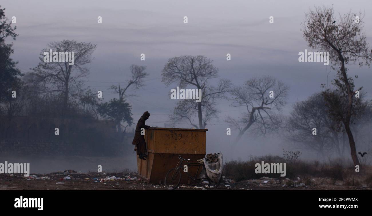 A Pakistani man looks inside a garbage container while collecting items ...