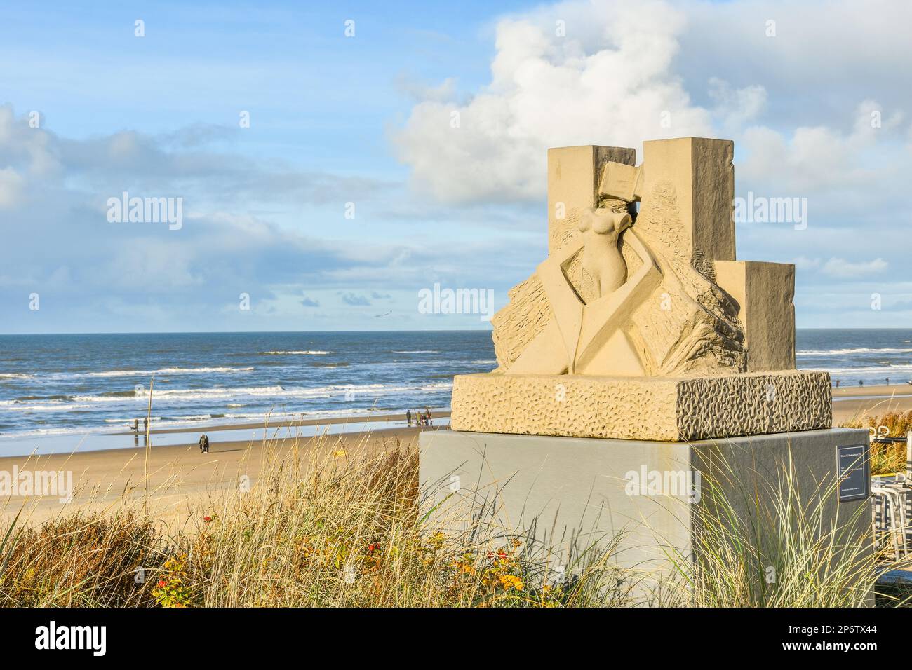 a statue on the beach next to the ocean with people in the water and ...