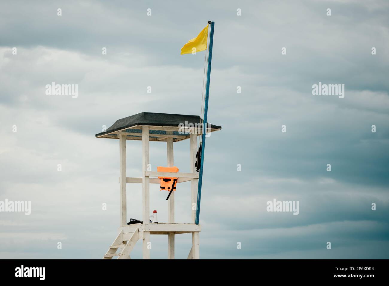 Empty white lifeguard tower with a yellow flag on the beach in windy ...