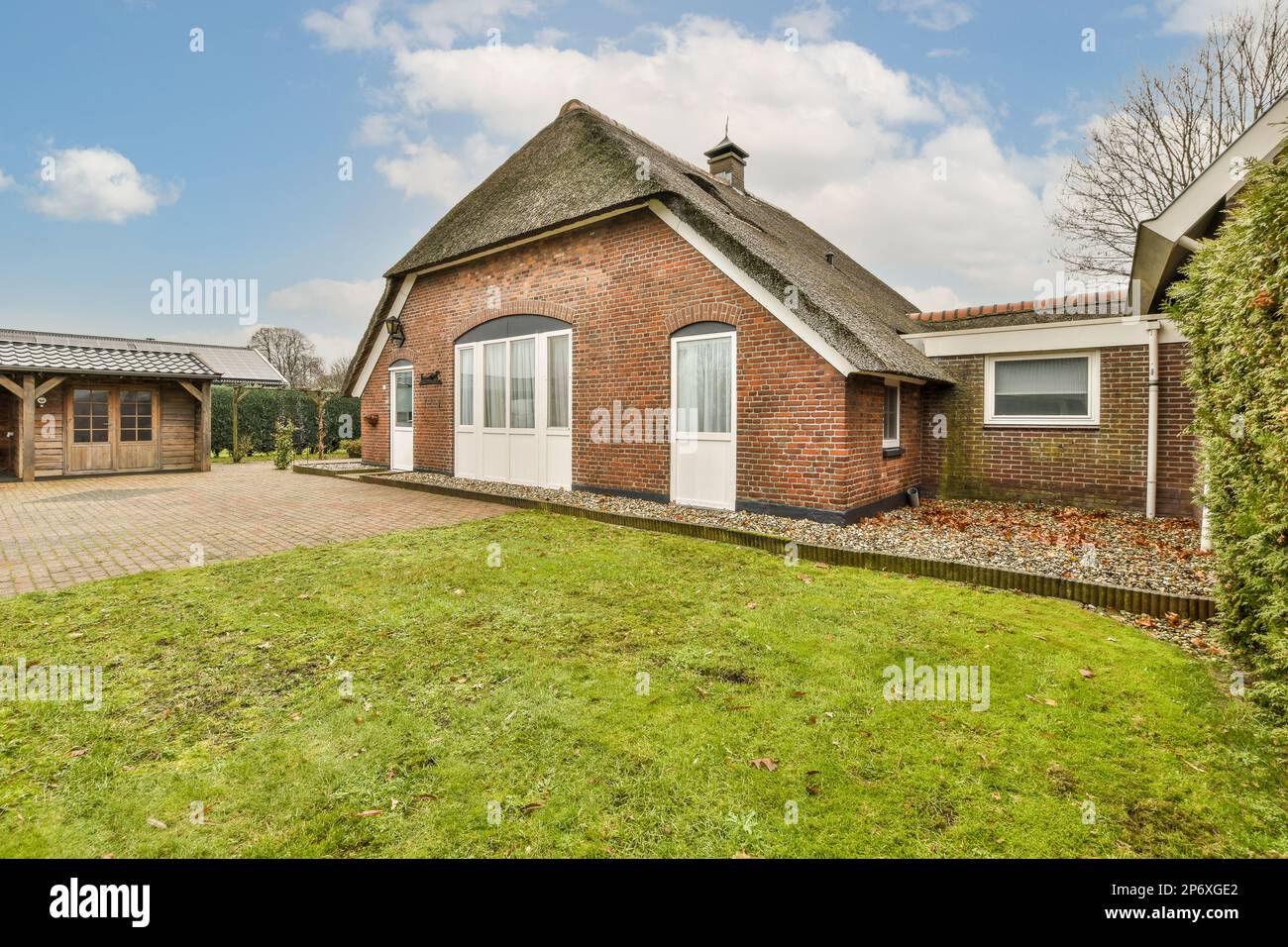 a house with a thatched roof and brick walls, surrounded by green grass ...