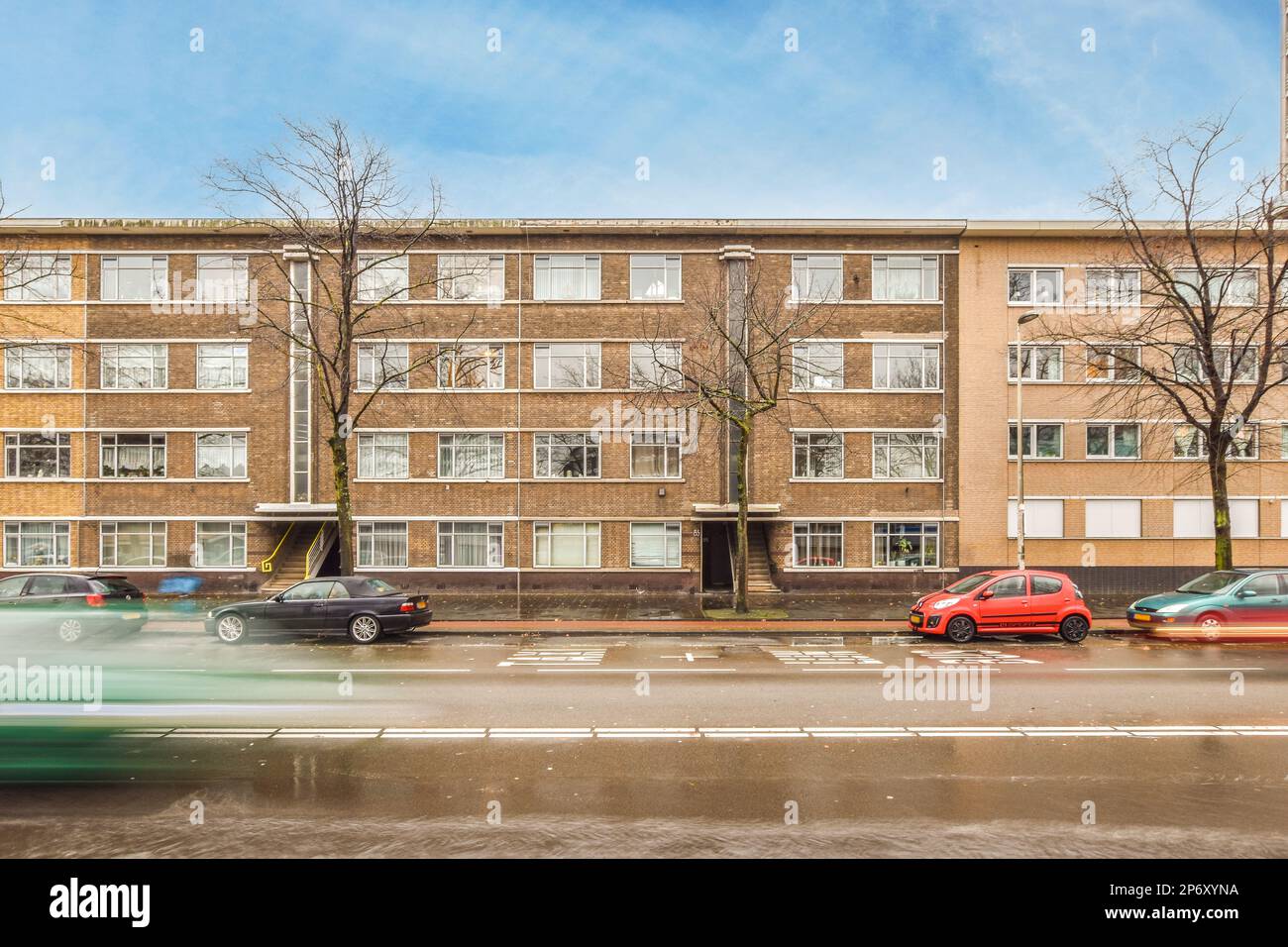 cars driving down the street in front of a multi - story apartment ...