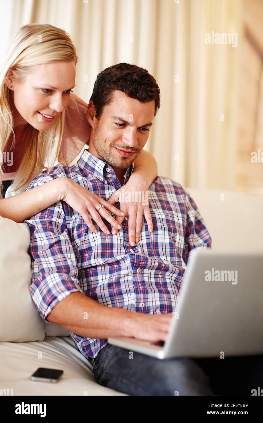 Keeping in touch with friends. A beautiful woman hugging her husband from behind while he sits ...