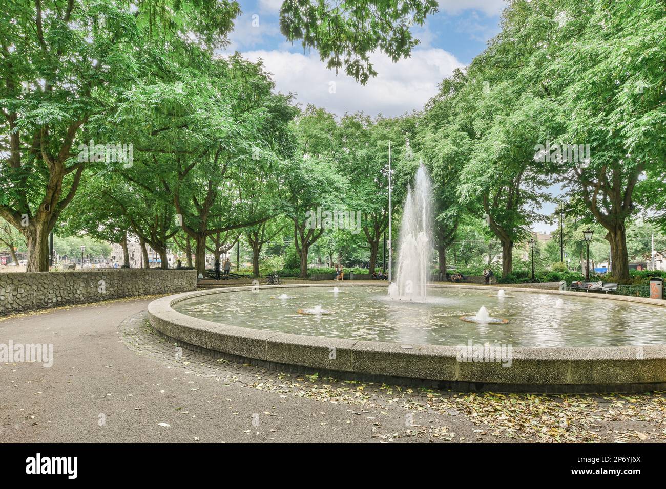 a fountain in the middle of a park with trees surrounding it and people ...