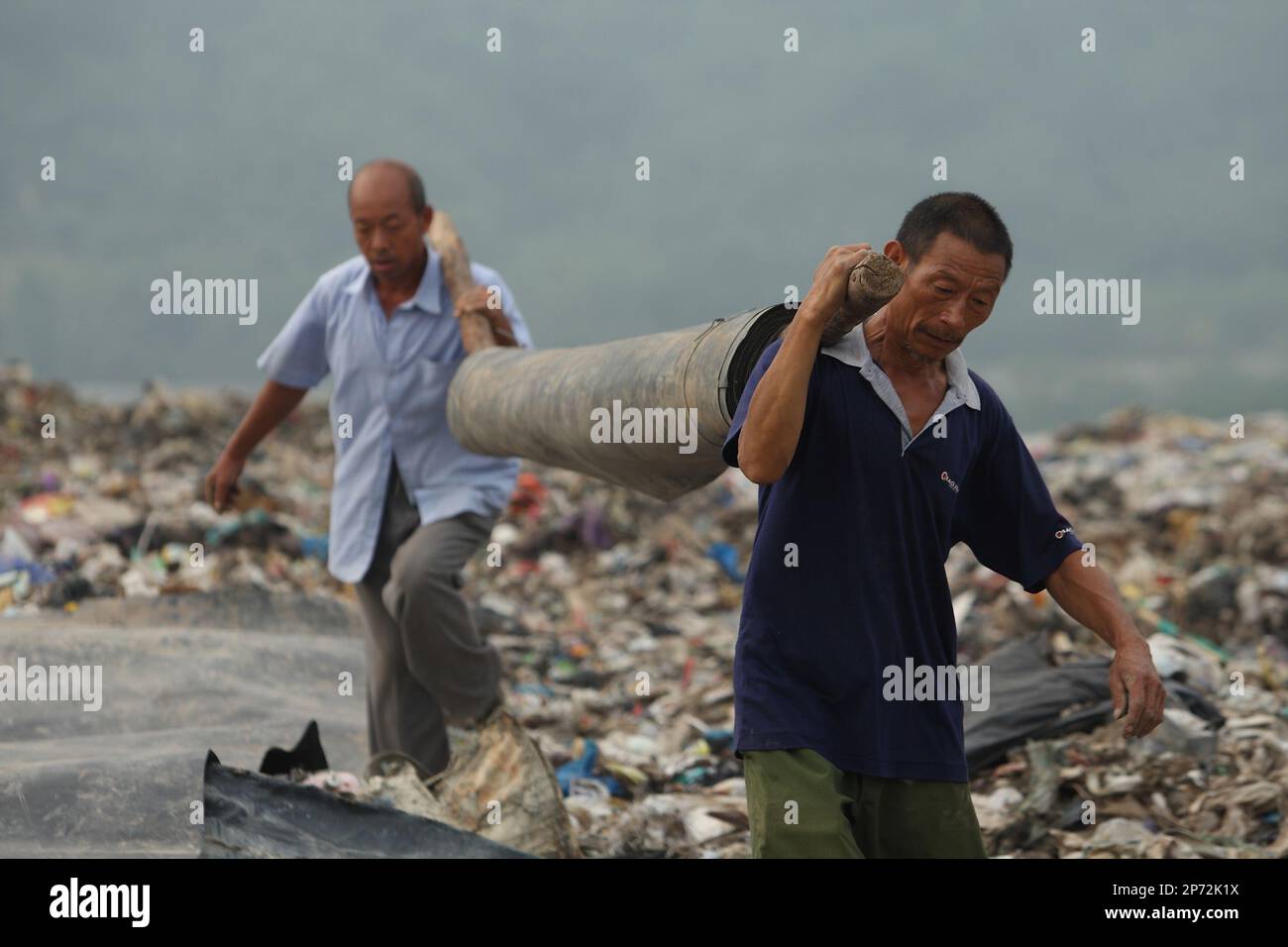 Workers cover the solid waste with plastic film at the Chengdu Solid ...