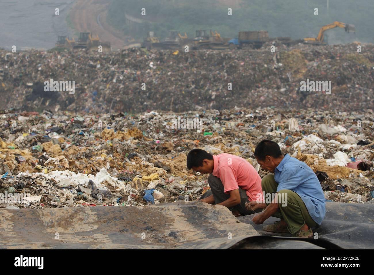 Workers cover the solid waste with plastic film at the Chengdu Solid ...