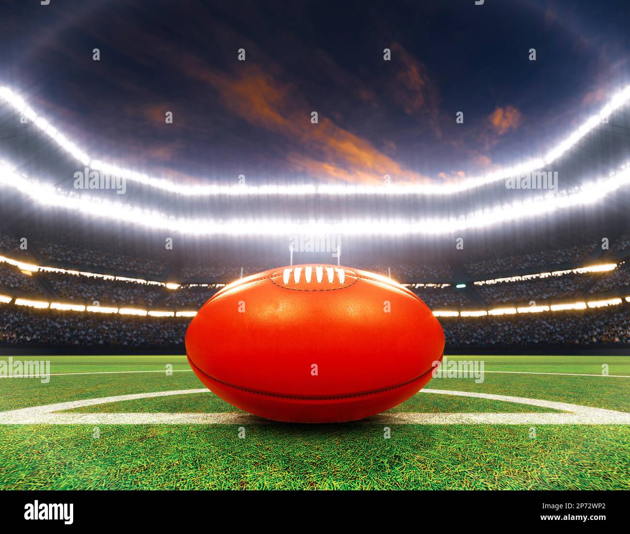 A red aussie rules ball on the center line of a stadium with posts on a ...