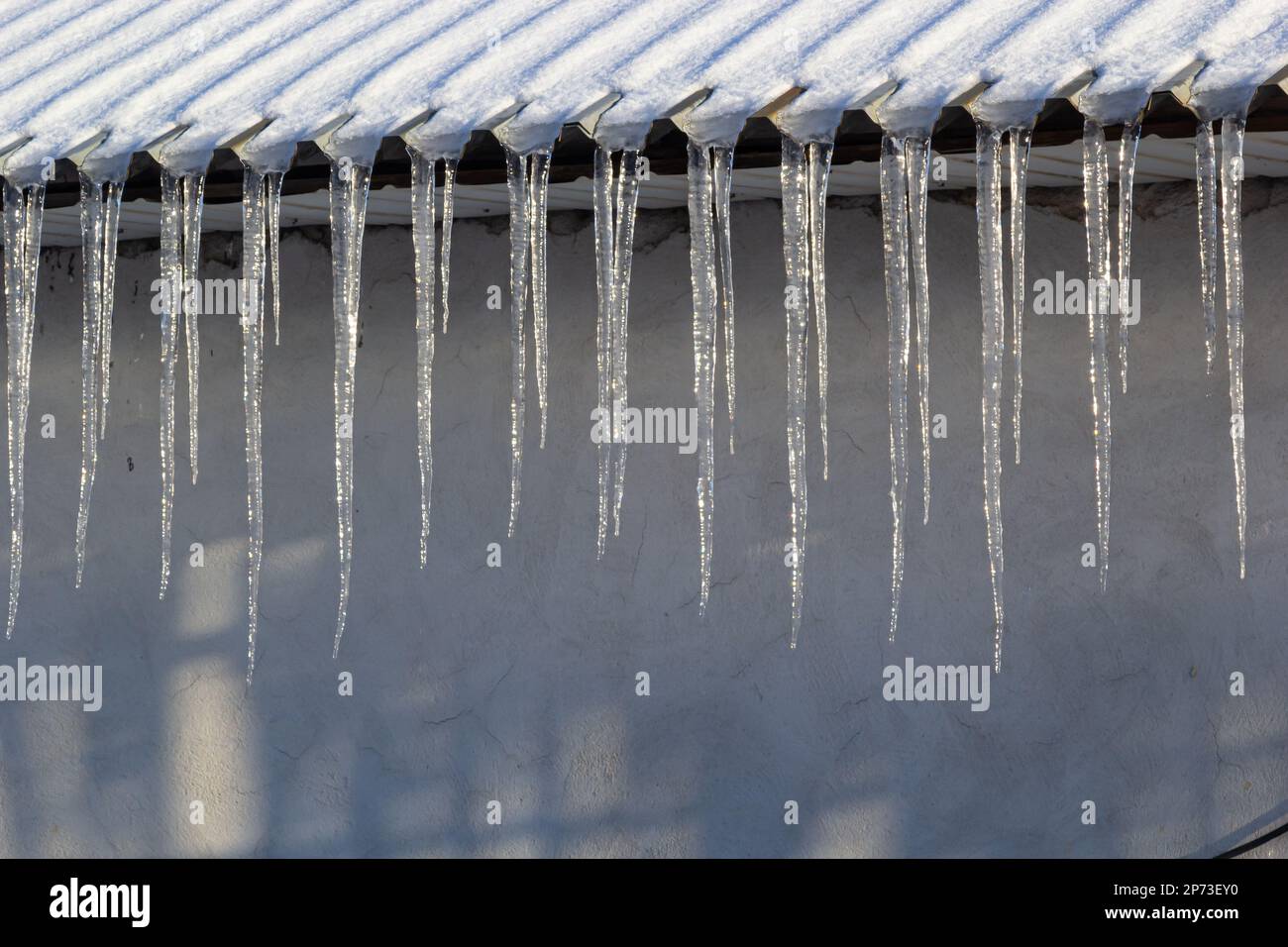 Sharp icicles and melted snow hanging from the eaves of the roof ...