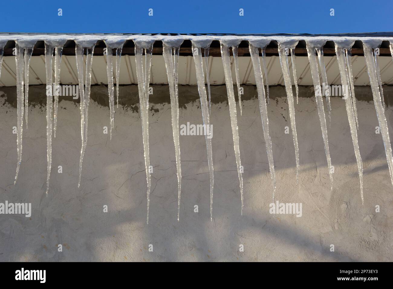 Sharp icicles and melted snow hanging from the eaves of the roof ...