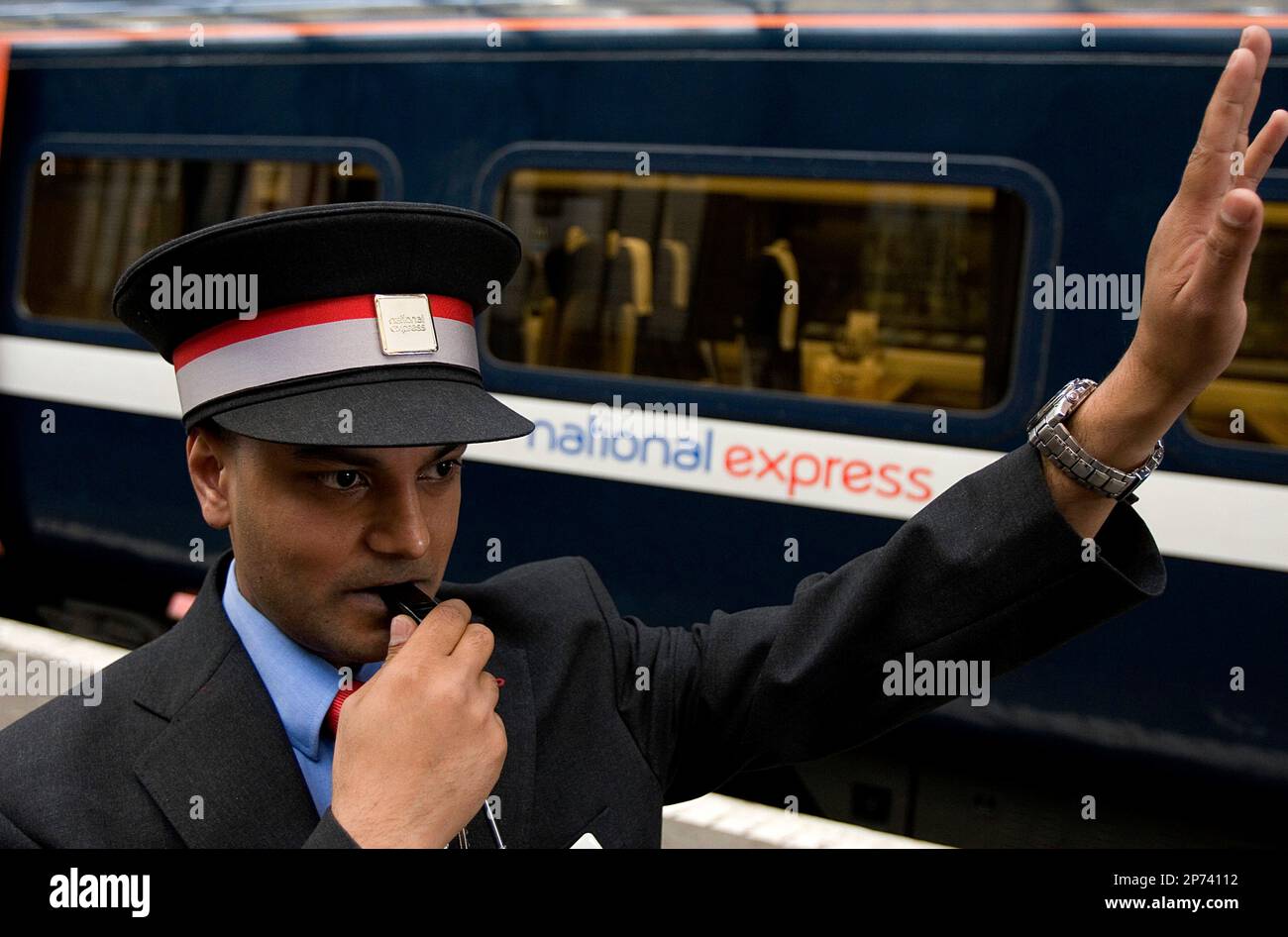 A train guard signals beside a National Express train at Kings Cross ...