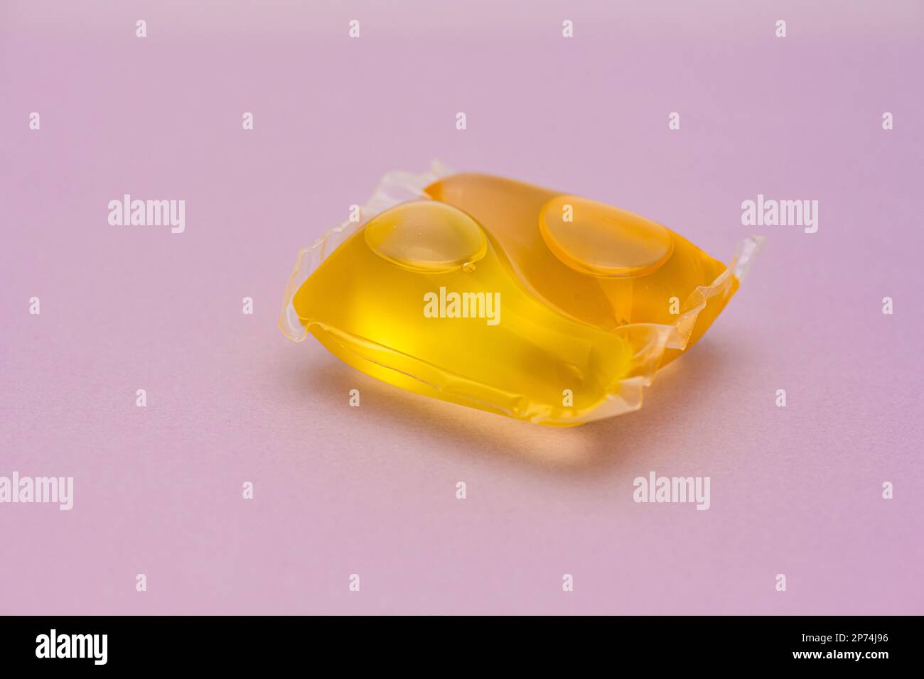 Yellow washing detergent capsule on purple table Stock Photo - Alamy