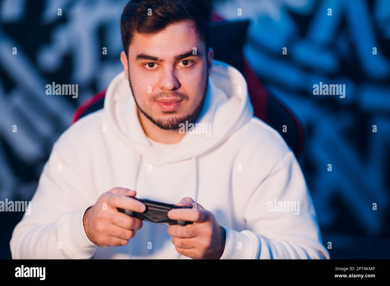 Young man plays on game console with gamepad looking to camera monitor ...