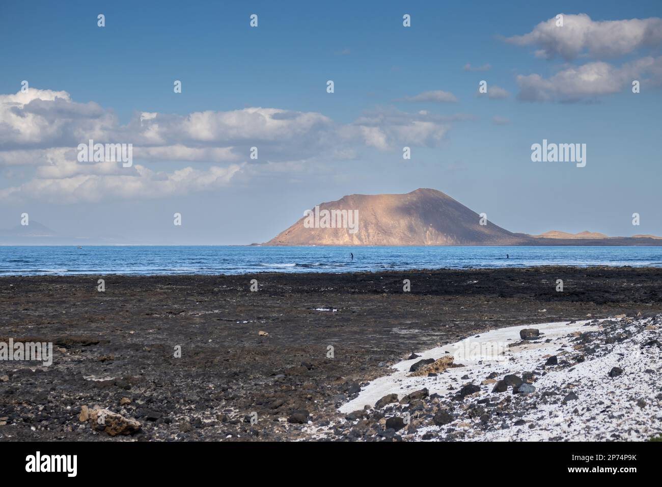 Dark lava soil on the beach and white pieces of coral. Calm Atlantic ...