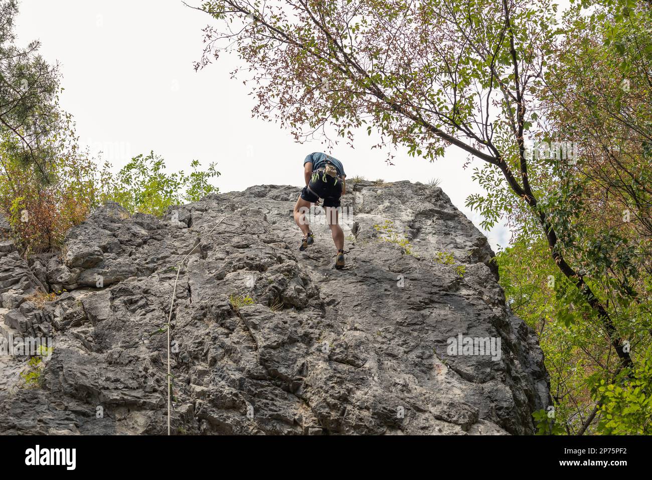Wide shot od a male climber hanging on a rope while ascending the rock ...
