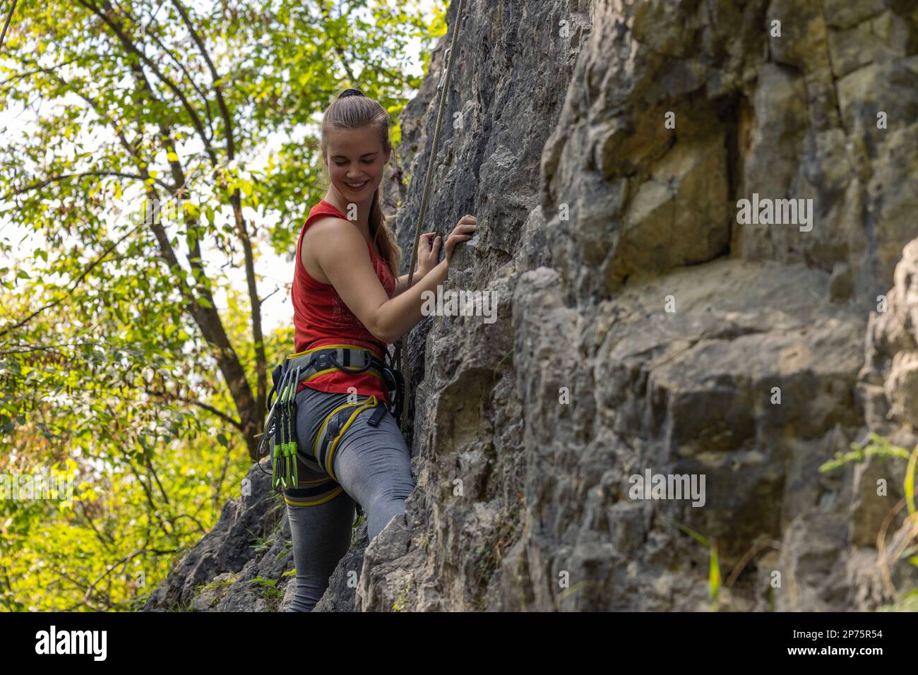 Female climber smiling and looking down while climbing in the rock wall ...