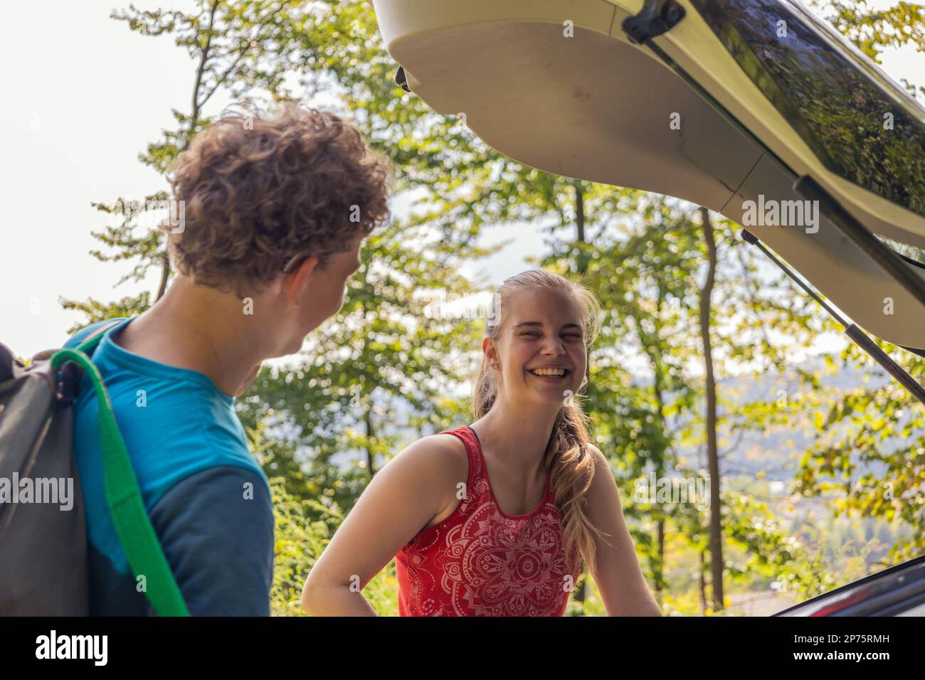 Female climber laughing while taking gear out of the car and talking to ...