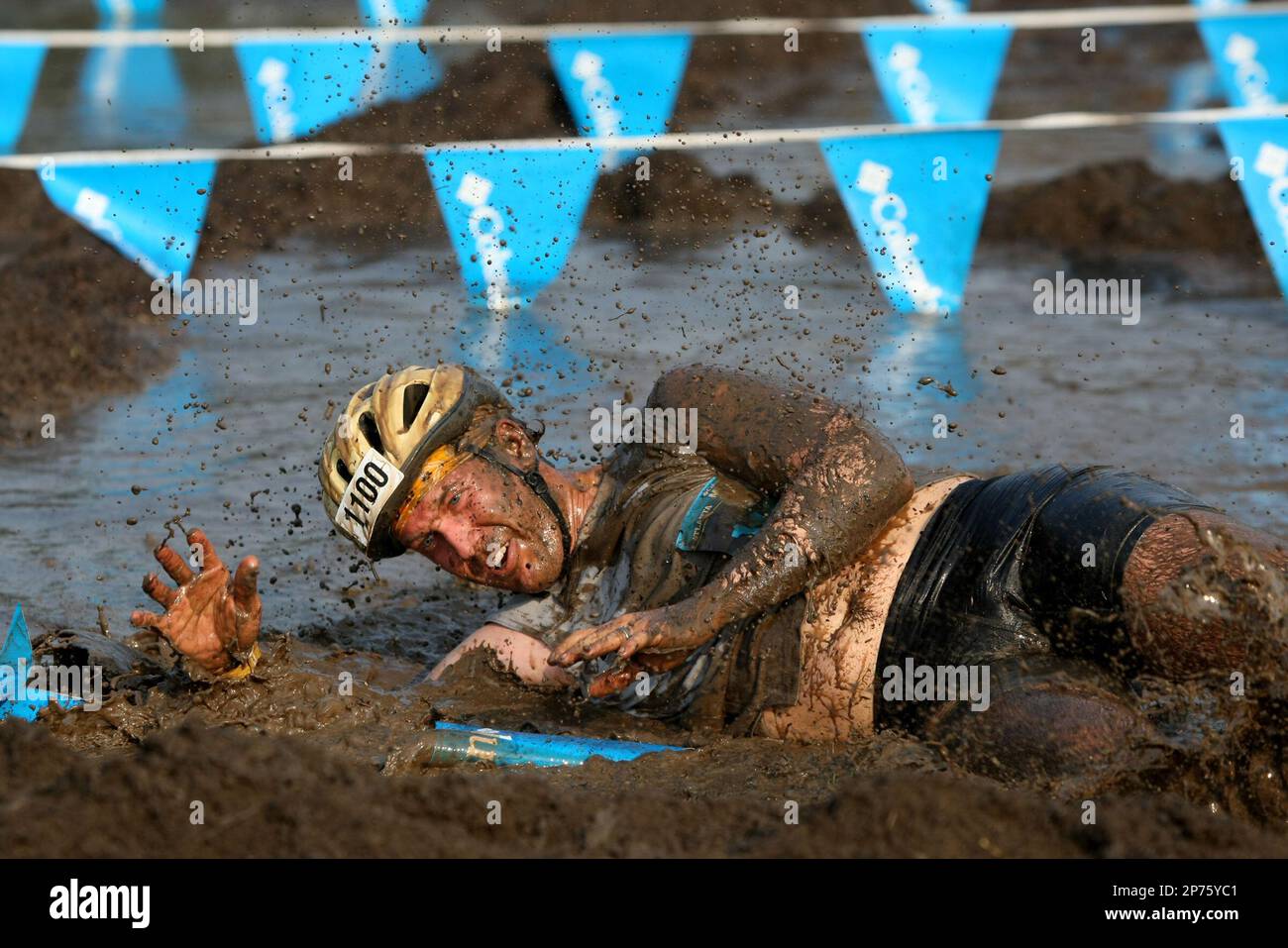 A competitor rolls under the lines of flags in the mud pit during the ...