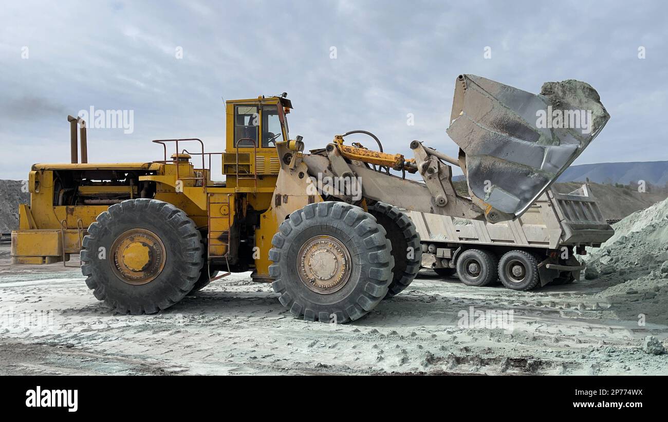 Wheel Loader loading soil on trucks, working at a huge mining site ...