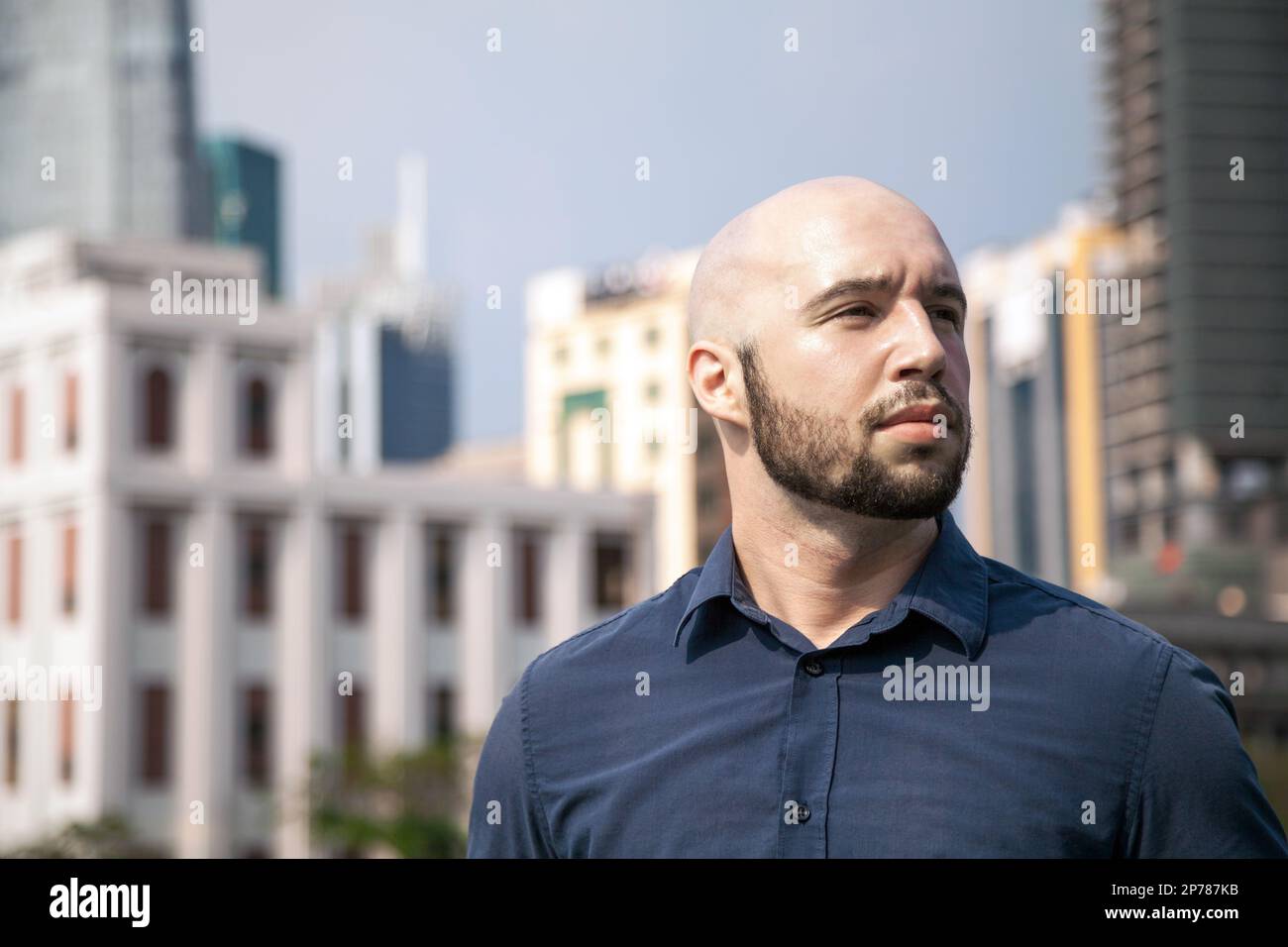 Serious attractive man standing against a cityscape and thinking. Bald ...