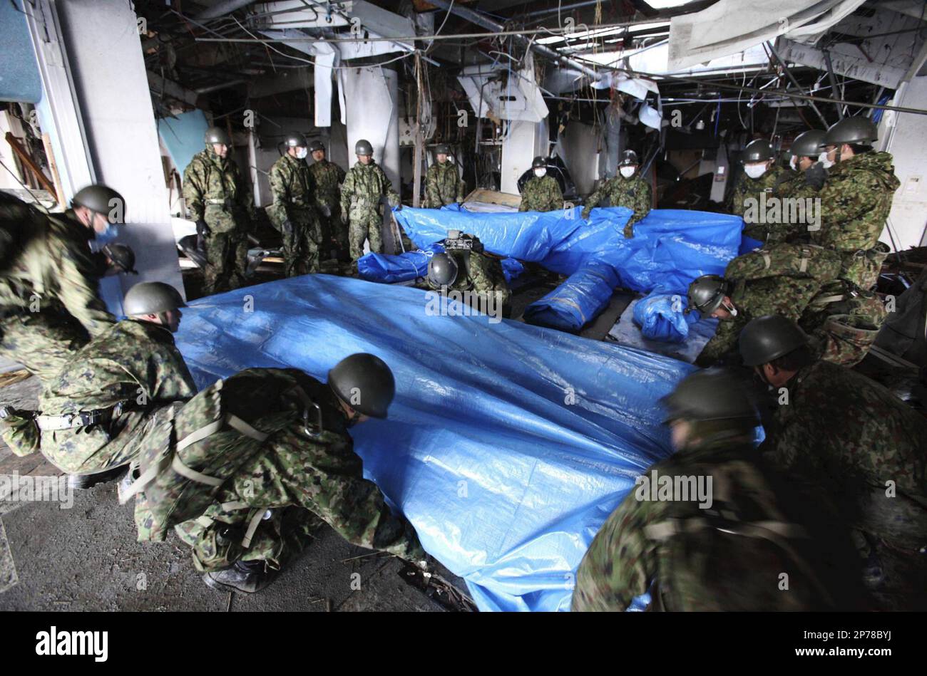 Self-Defense Force members put a tarp over bodies in Minamisanriku ...