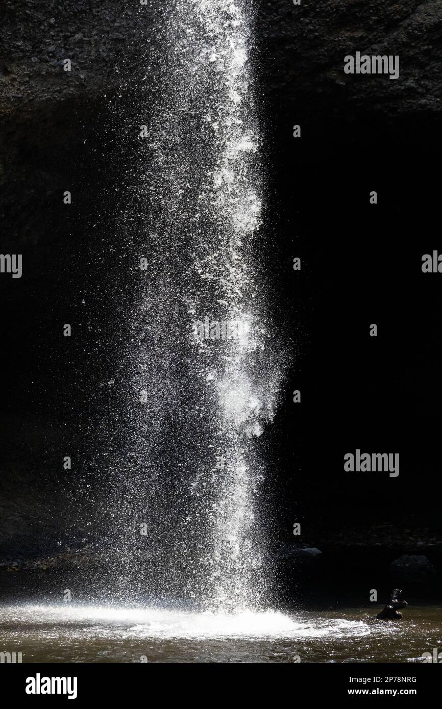 Splashing waterfall drop on pond with dark background of cave in summer ...
