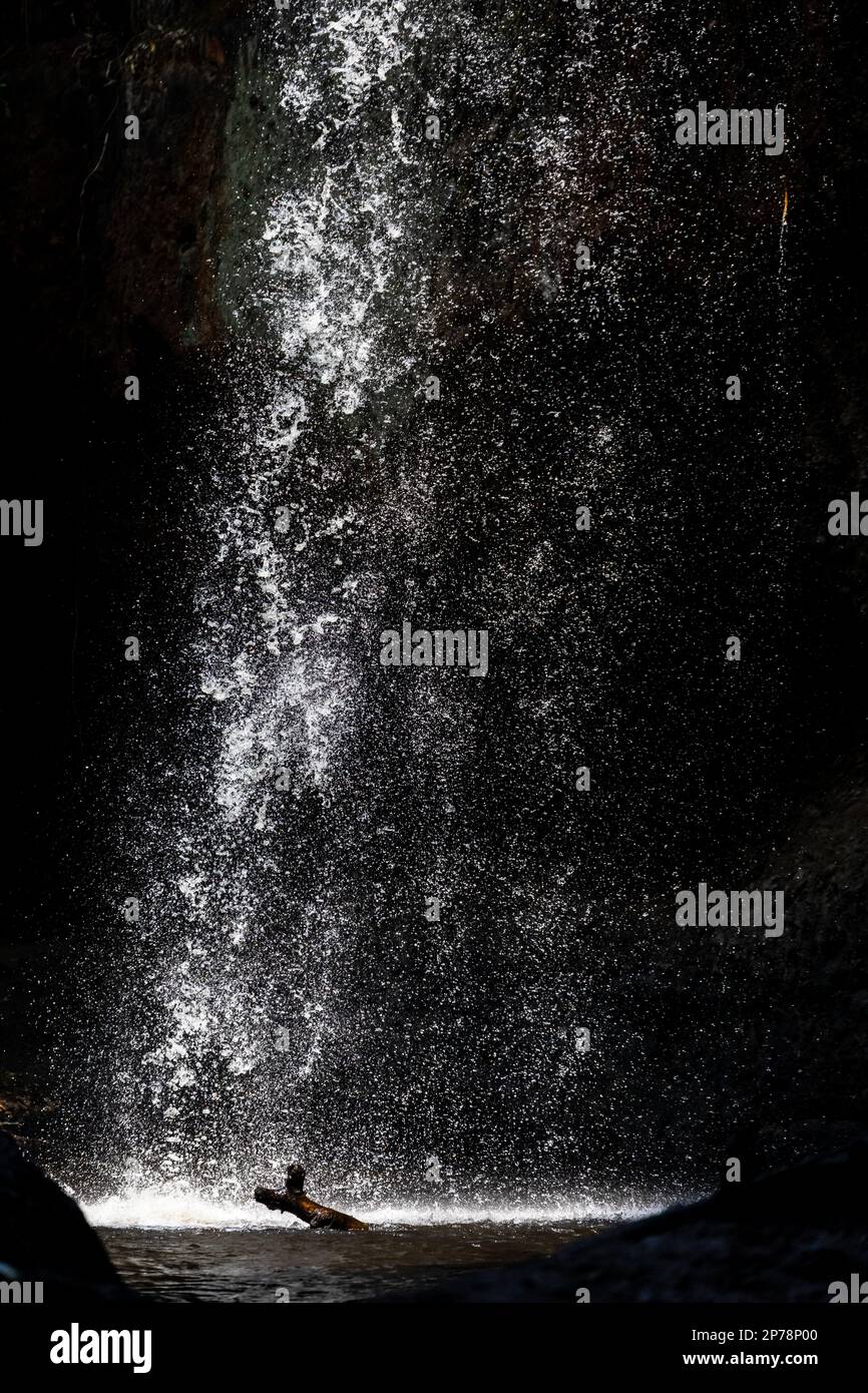 Splashing waterfall drop on pond with dark background of cave in summer ...