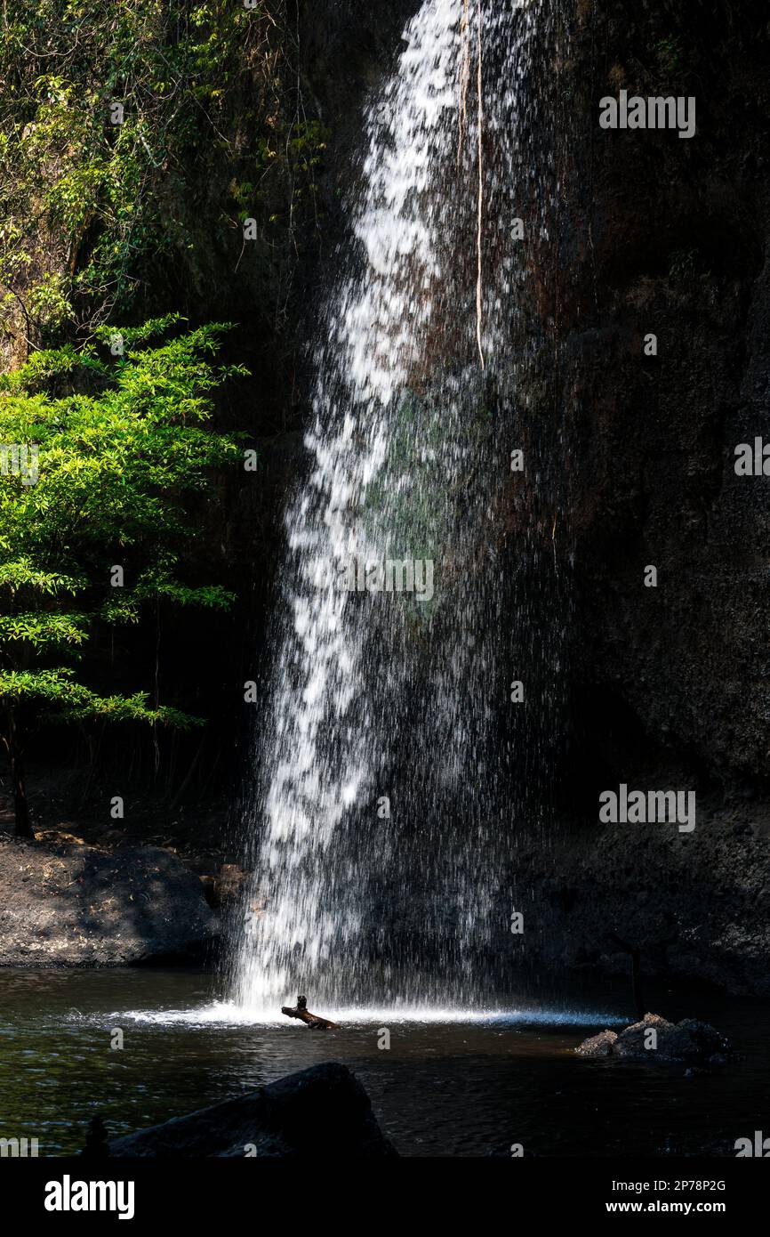 Splashing waterfall drop on pond with dark background of cave inside ...
