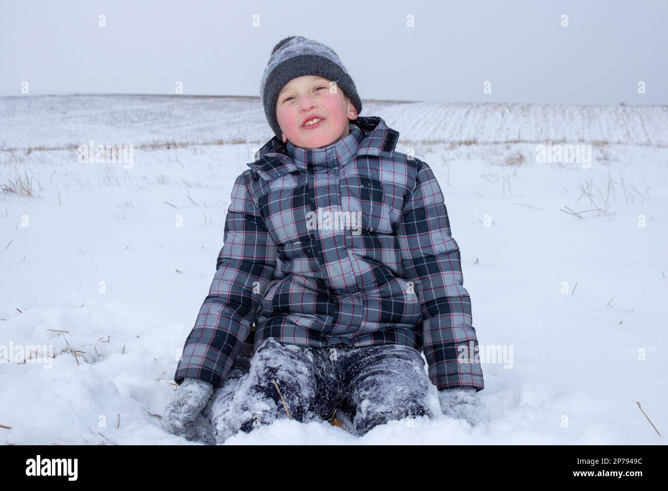 happy boy in winter with rosy cheeks sits in the snow Stock Photo - Alamy
