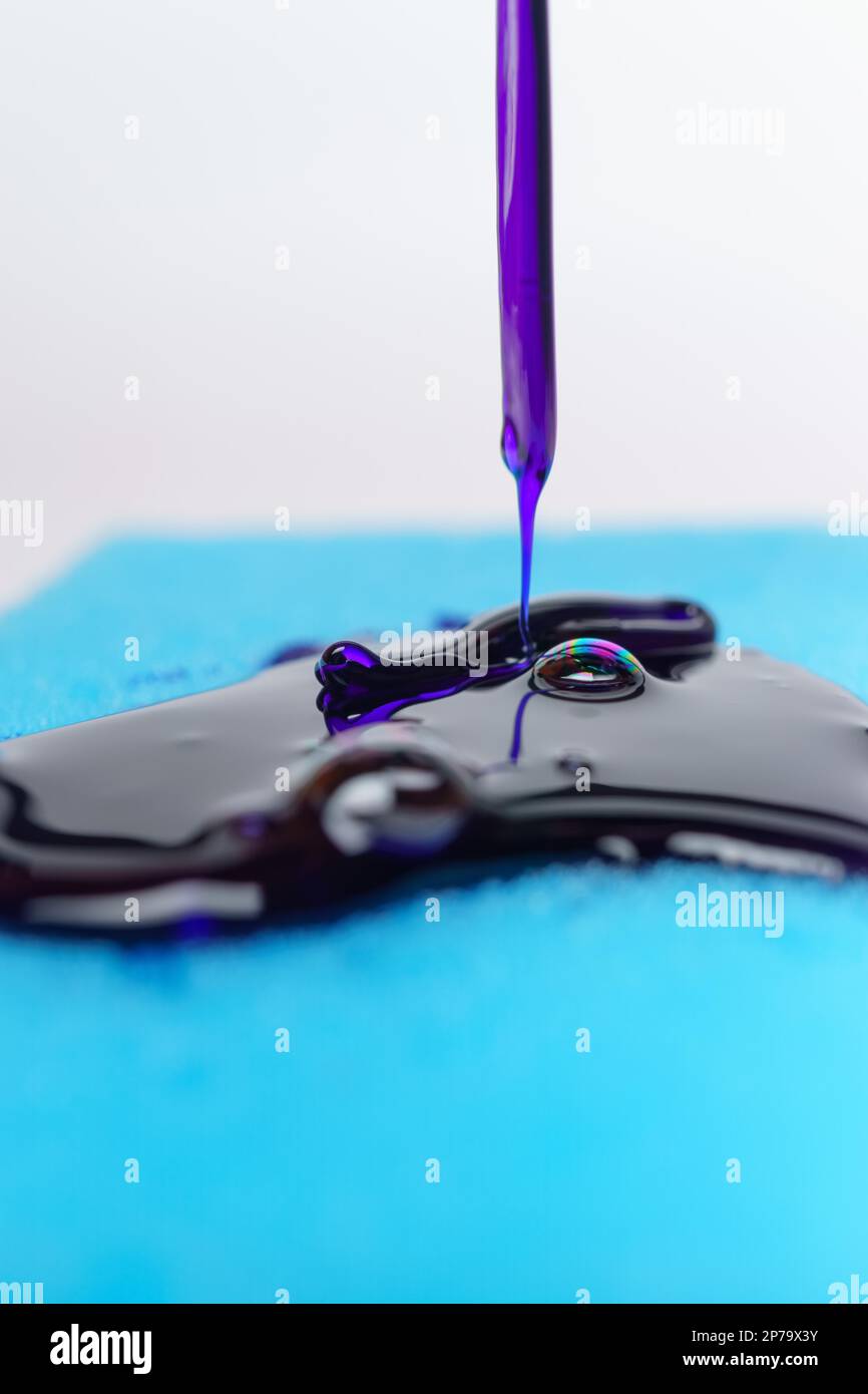 Purple liquid soap dripping on a blue sponge on a white background ...