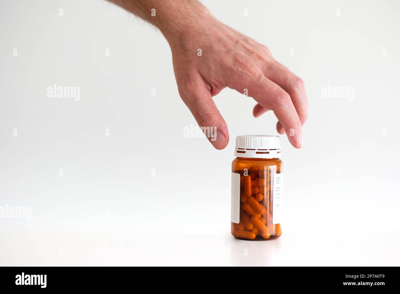 Caucasian male hand reaching out to grab a plastic medical pills bottle ...