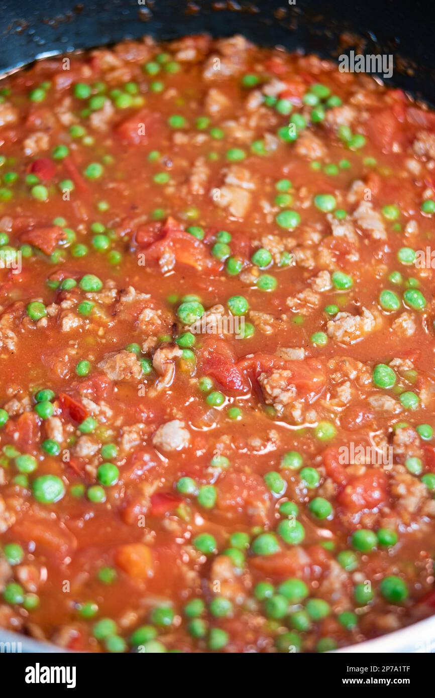Italian tomato sauce ragu with fresh green peas in a large pan close up ...