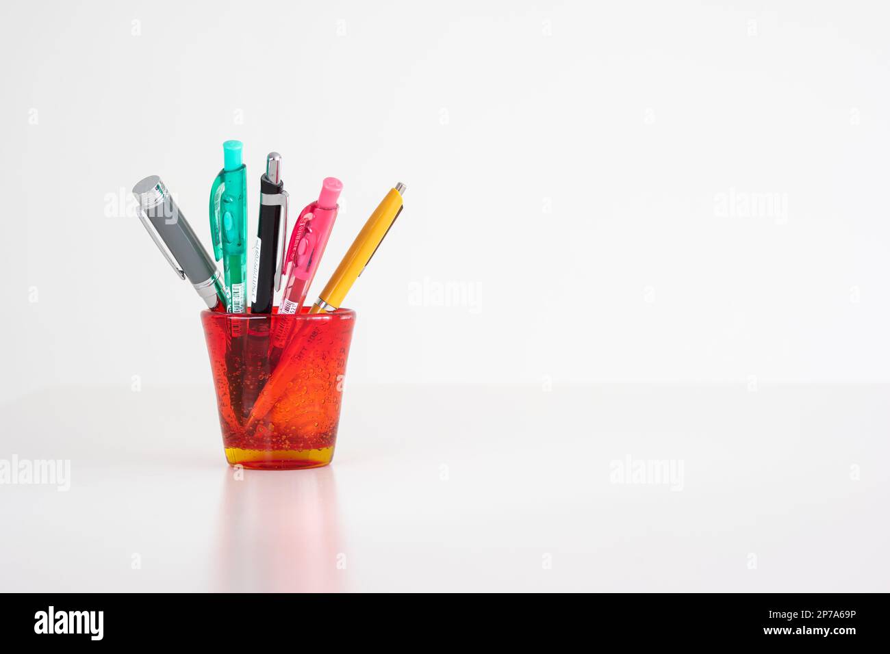 Different colorful pens in a red stained-glass cup isolated on white ...