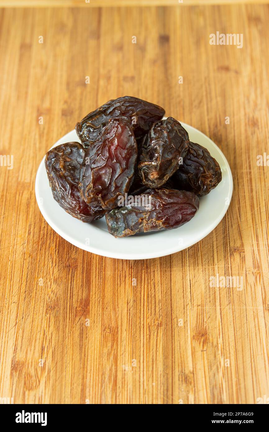 Big pitted dried dates on a small white plate set on a wooden boar top ...
