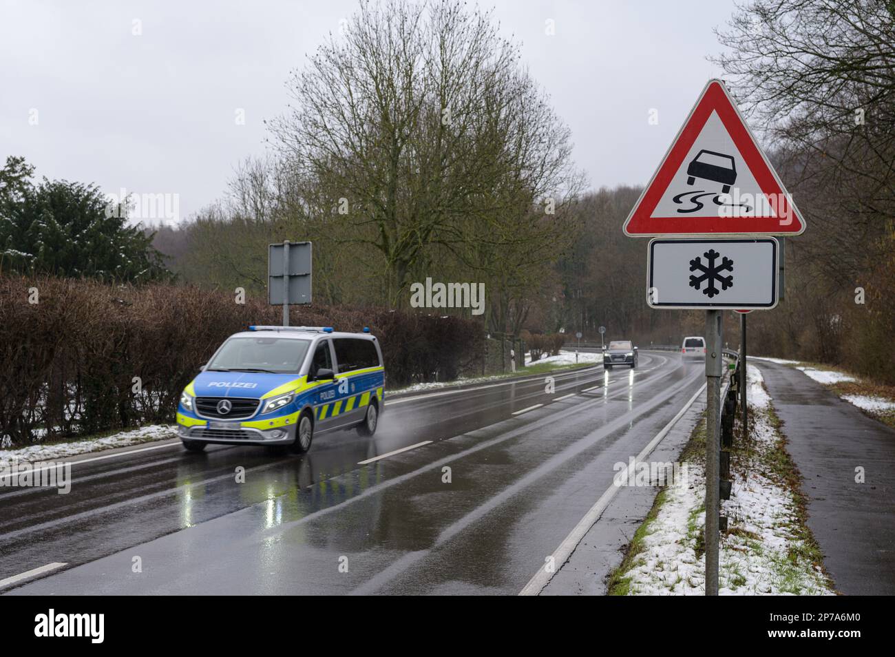 Police car driving down wet road in winter with ice warning sign ...