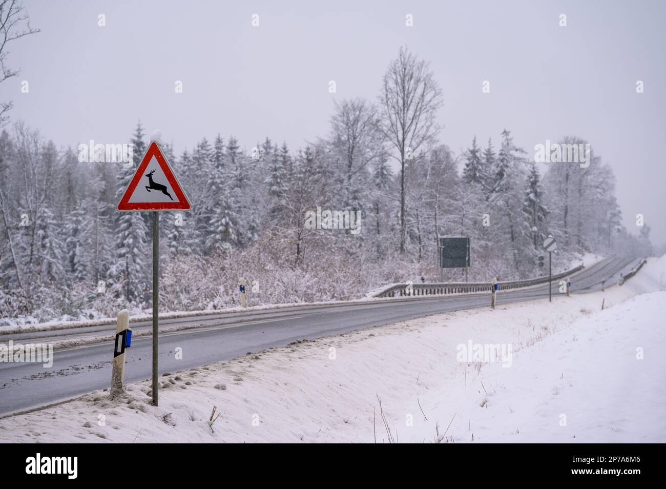 Road sign indicating deer and animals crossing in snow next to rural ...