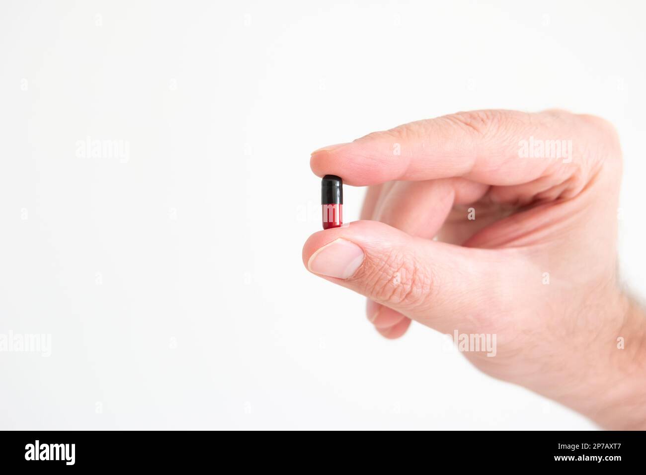 Caucasian male hand holding a medical black and red capsule pill ...