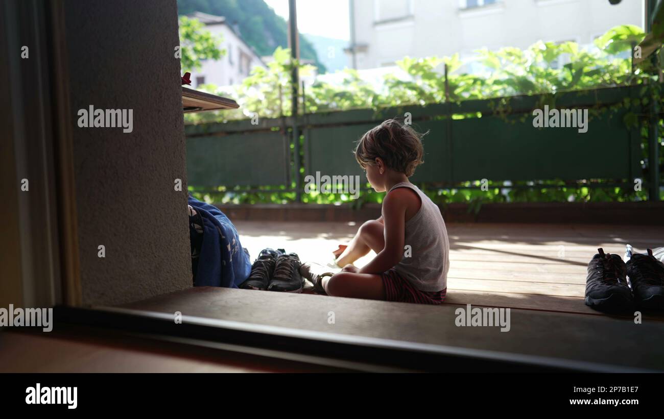 One small boy putting shoes on by doorstep ready to go out. Kid getting ...