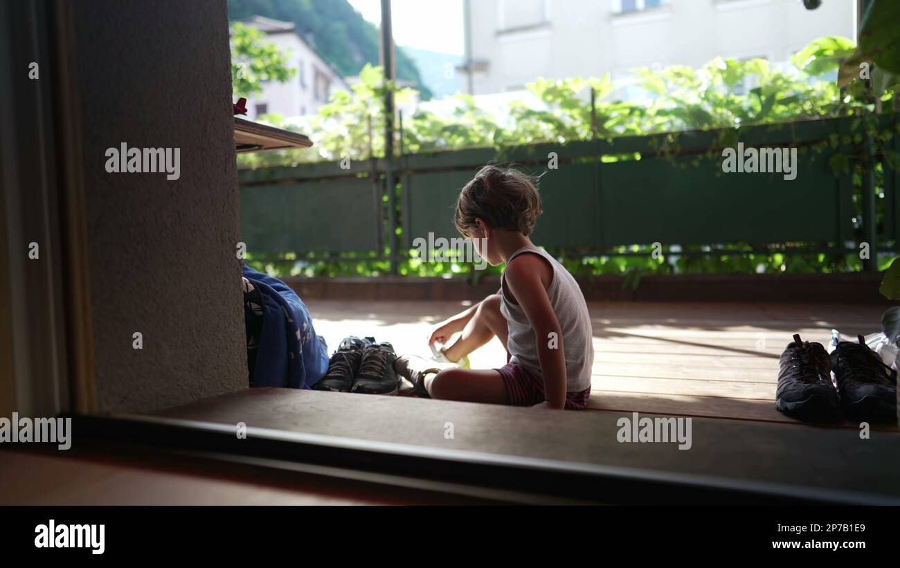 One small boy putting shoes on by doorstep ready to go out. Kid getting ...