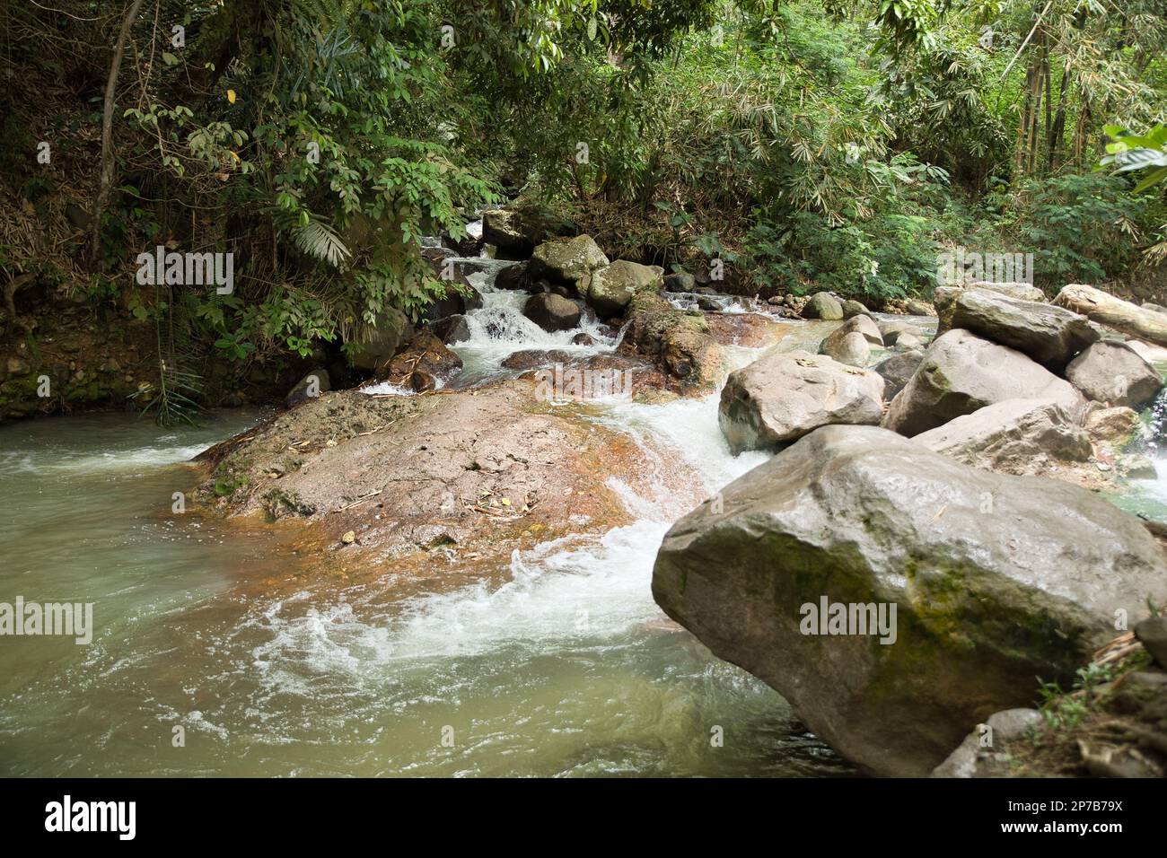 Peaceful shot of the hot spring of Malanage on Flores flowing down rocks surrounded by ...