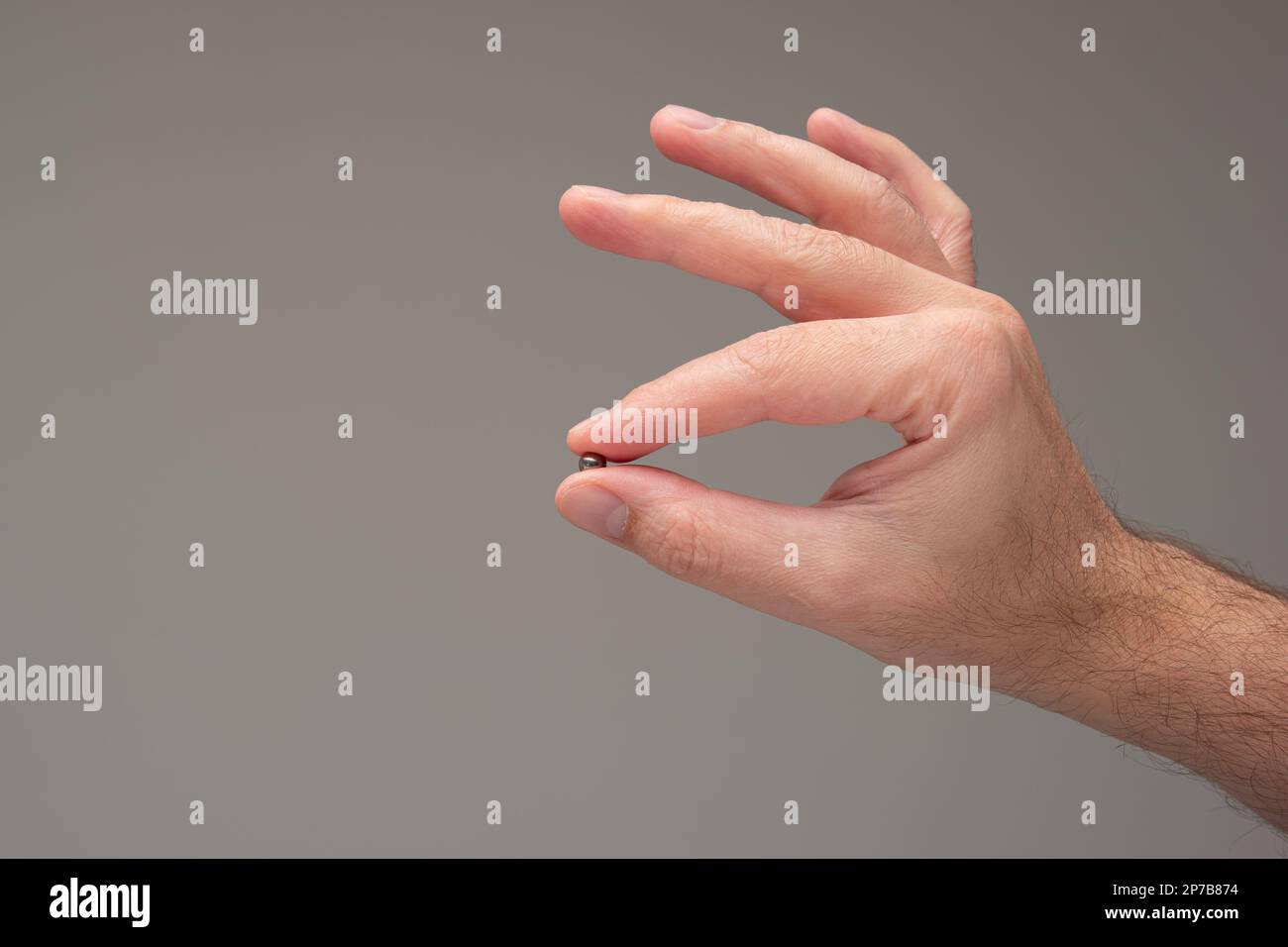 Very small metal bearing ball held between fingers by Caucasian male ...